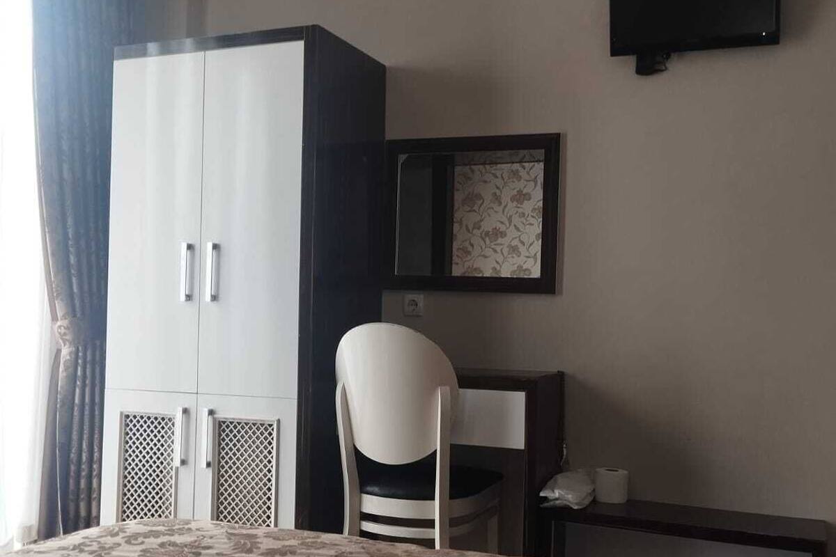 Quarto com uma cama grande, guarda-roupa, escrivaninha, cadeira e televisão na parede.