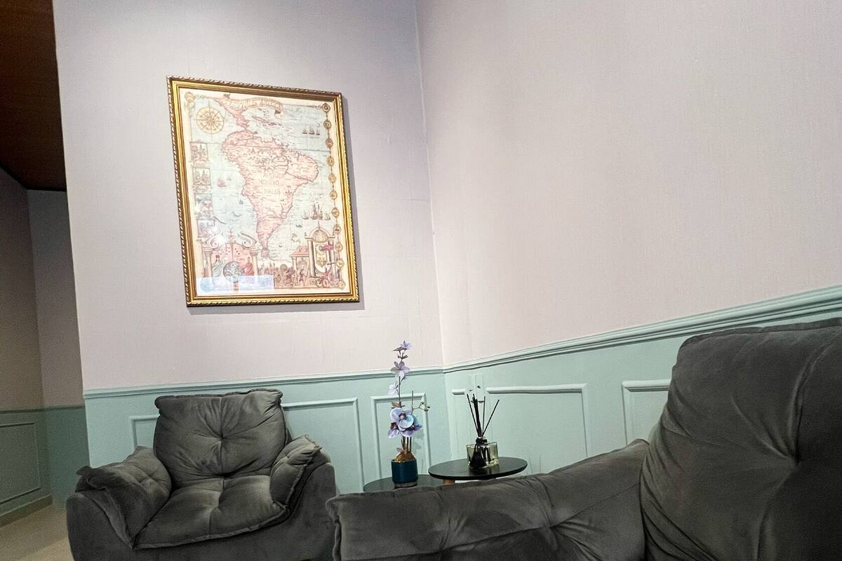 Um quarto com dois sofás cinzentos, um mapa emoldurado na parede e uma mesinha com um vaso e uma vela.