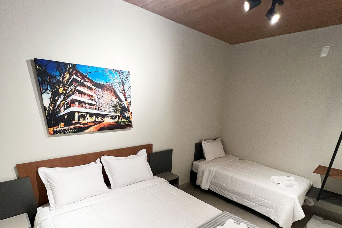 Quarto de hotel com duas camas, um quadro na parede e uma luminária no teto.