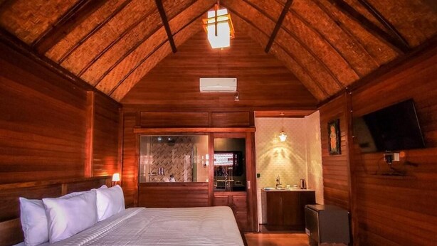 Quarto de cabana de madeira com uma cama, uma secretária pequena, uma televisão e um banheiro com chuveiro.