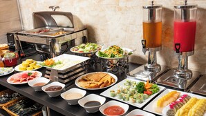 Um buffet com diversos itens de comida, incluindo saladas, carnes e sobremesas, além de dispensadores de bebidas.