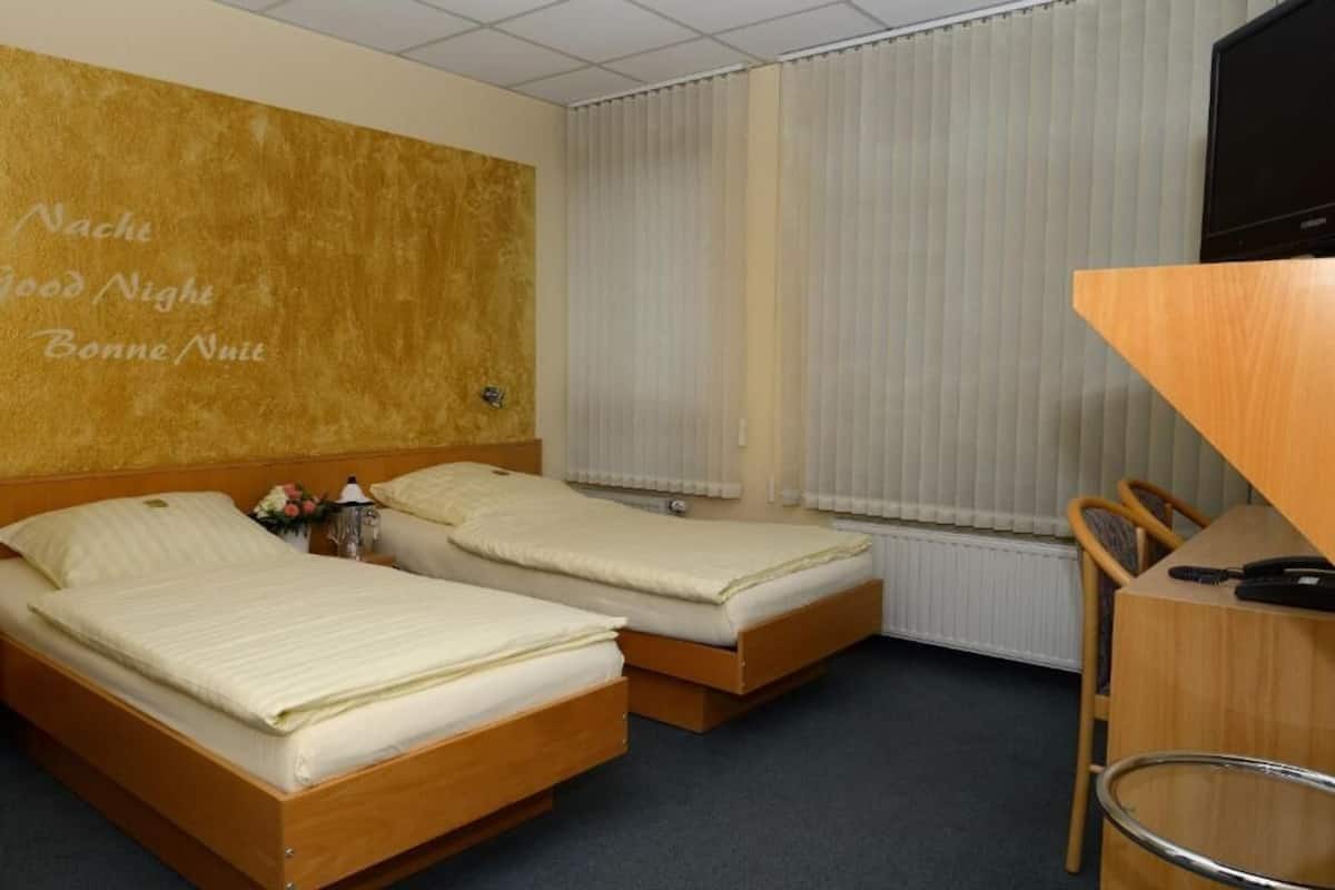 Quarto de hotel com duas camas, uma mesa, uma cadeira, uma televisão e uma janela com persianas.