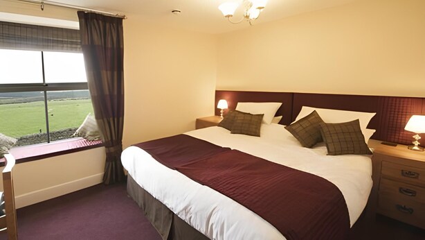Quarto de hotel com cama grande, escrivaninha e janela com cortinas.