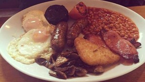 Um prato de comida com ovos, salsichas, feijão, cogumelos e um pedaço de carne.