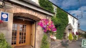 Um edifício de pedra com porta de madeira, placa indicando restaurante e plantas em vasos.