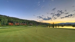 Um campo de golfe com a marcação central, rodeado por relva bem cuidada e um corpo de água que reflete o céu.