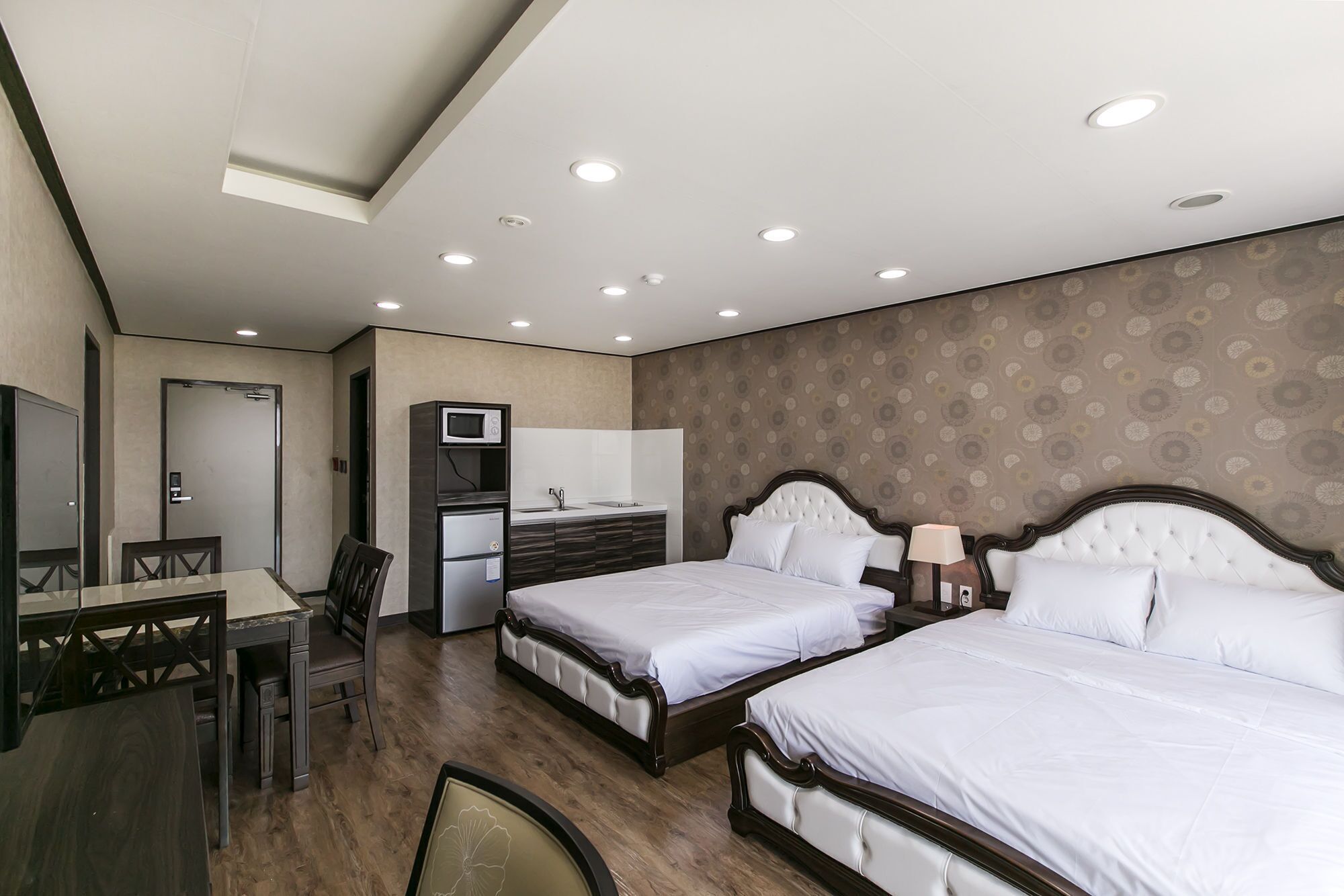 Quarto de hotel com duas camas, uma escrivaninha, uma cadeira, micro-ondas e uma pequena cozinha equipada.