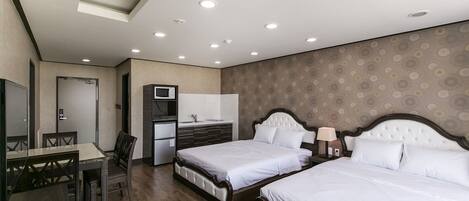 Quarto de hotel com duas camas, uma escrivaninha, uma cadeira, micro-ondas e uma pequena cozinha equipada.