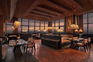 Restaurante moderno com pé direito alto, grandes janelas e diversas opções de assento, incluindo mesas e cabines.