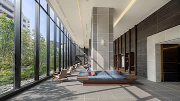 Interior moderno com grandes janelas, área de estar com sofás e cadeiras, e vista para o verde lá fora.