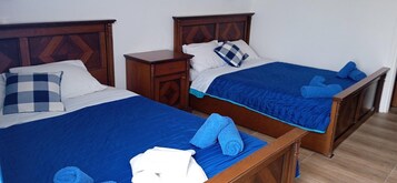 Duas camas de casal com cabeceiras de madeira, uma mesinha de cabeceira e roupa de cama azul.