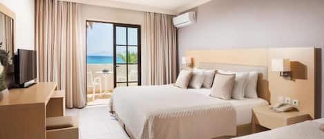 Quarto de hotel com duas camas, uma escrivaninha, uma televisão e vista para o mar.