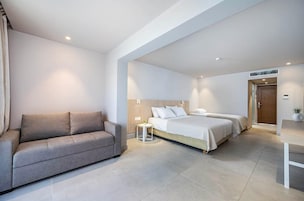 Quarto de hotel moderno com sofá, cama com duas almofadas, mesa lateral pequena e uma porta.