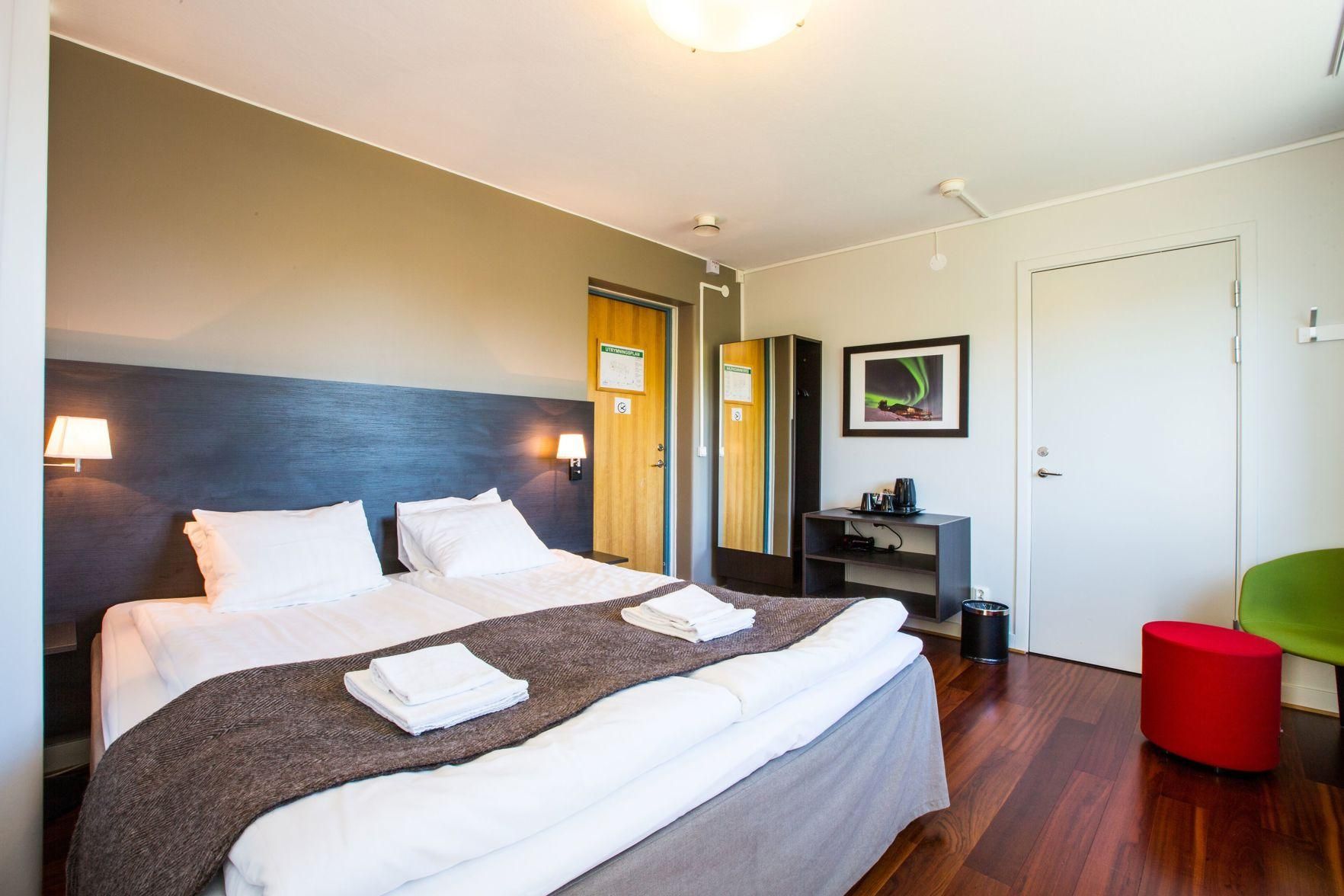 Quarto de hotel com uma cama grande, abajures, escrivaninha, cadeira e um quadro na parede.