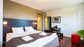 Quarto de hotel com uma cama grande, abajures, escrivaninha, cadeira e um quadro na parede.