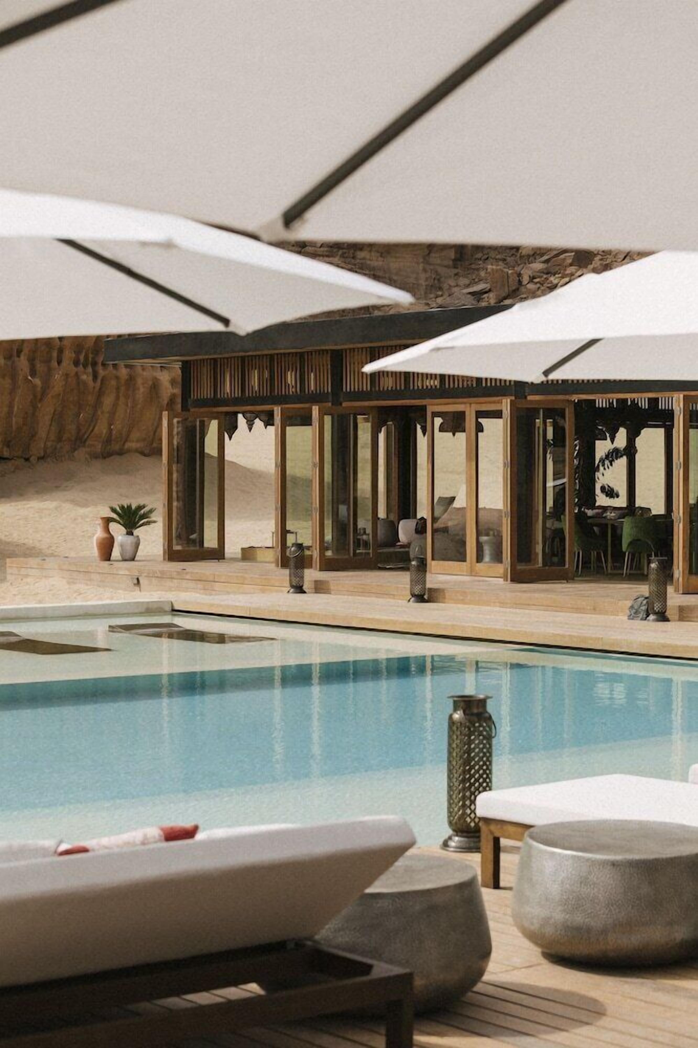 Uma área de piscina com espreguiçadeiras, um espaço de estar coberto e vista para a praia.
