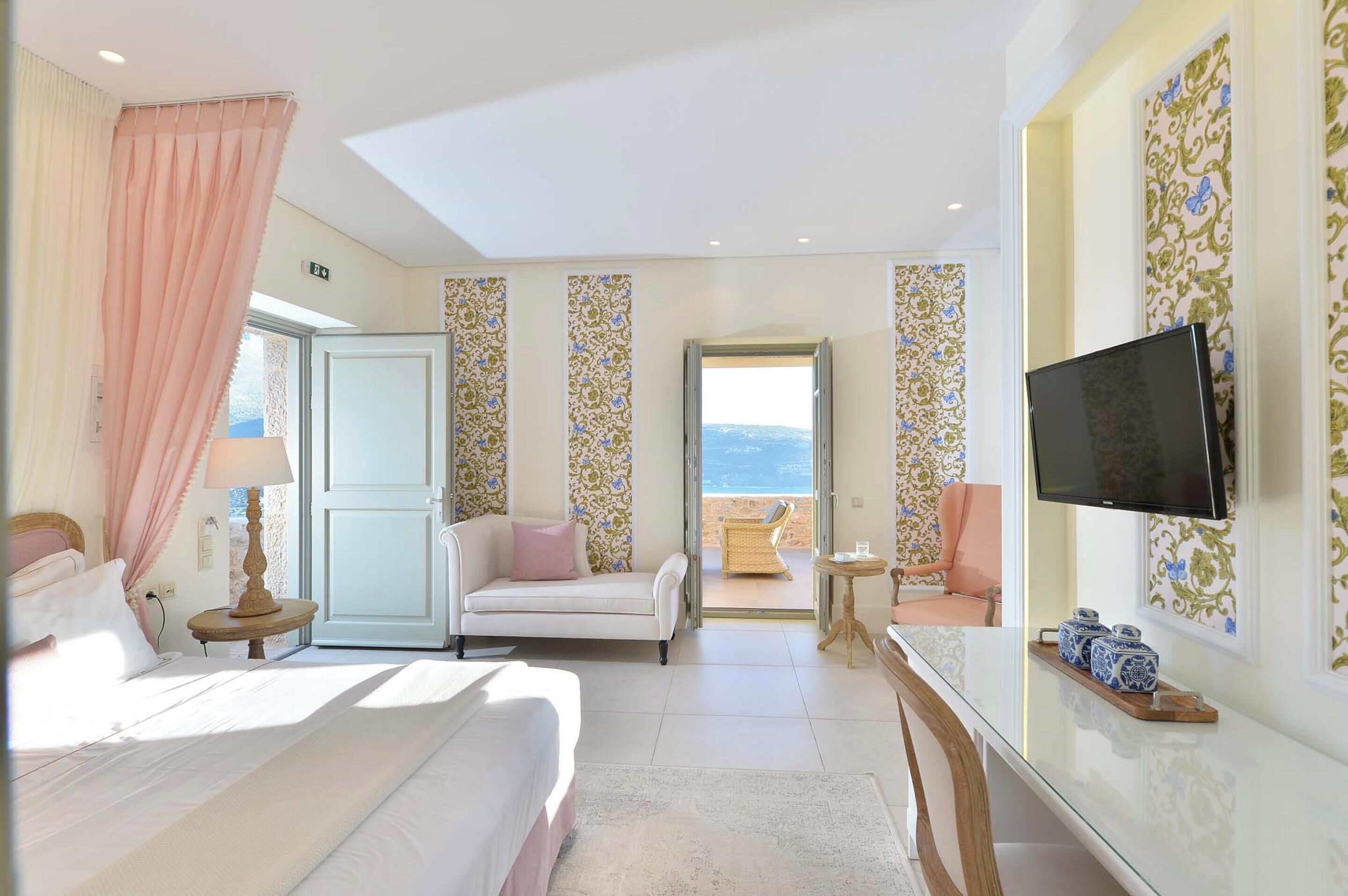 Quarto de hotel com cama, sofá, televisão e vista para o mar.