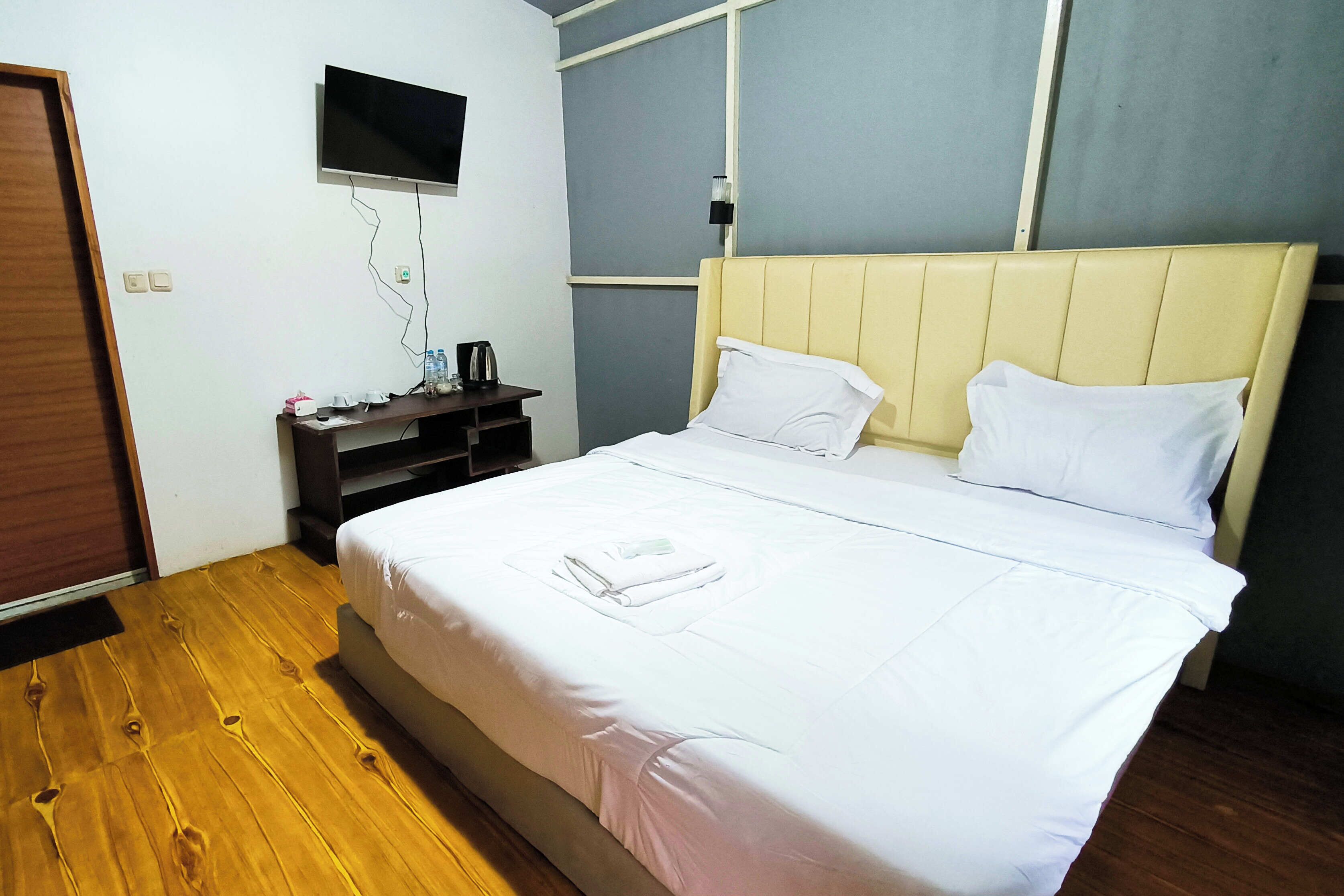 Quarto de hotel com uma cama, uma televisão presa à parede e piso de madeira.