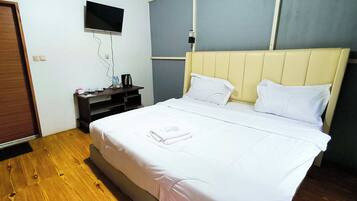 Quarto de hotel com uma cama, uma televisão presa à parede e piso de madeira.