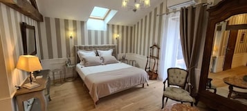 Quarto com cama grande, mesa de cabeceira, luminária, cadeira e janela com cortinas.