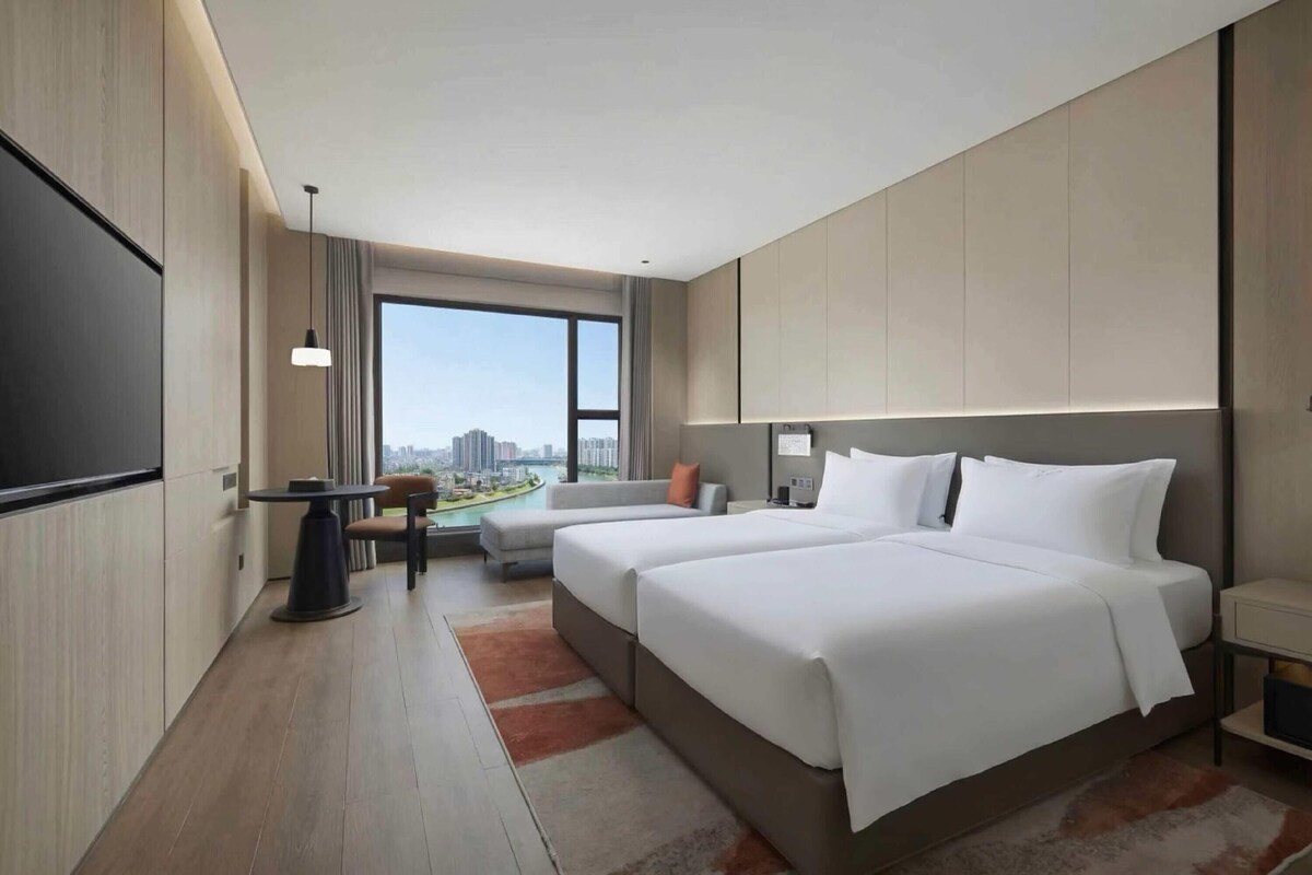 Quarto de hotel com uma cama grande, escrivaninha, cadeira e televisão.