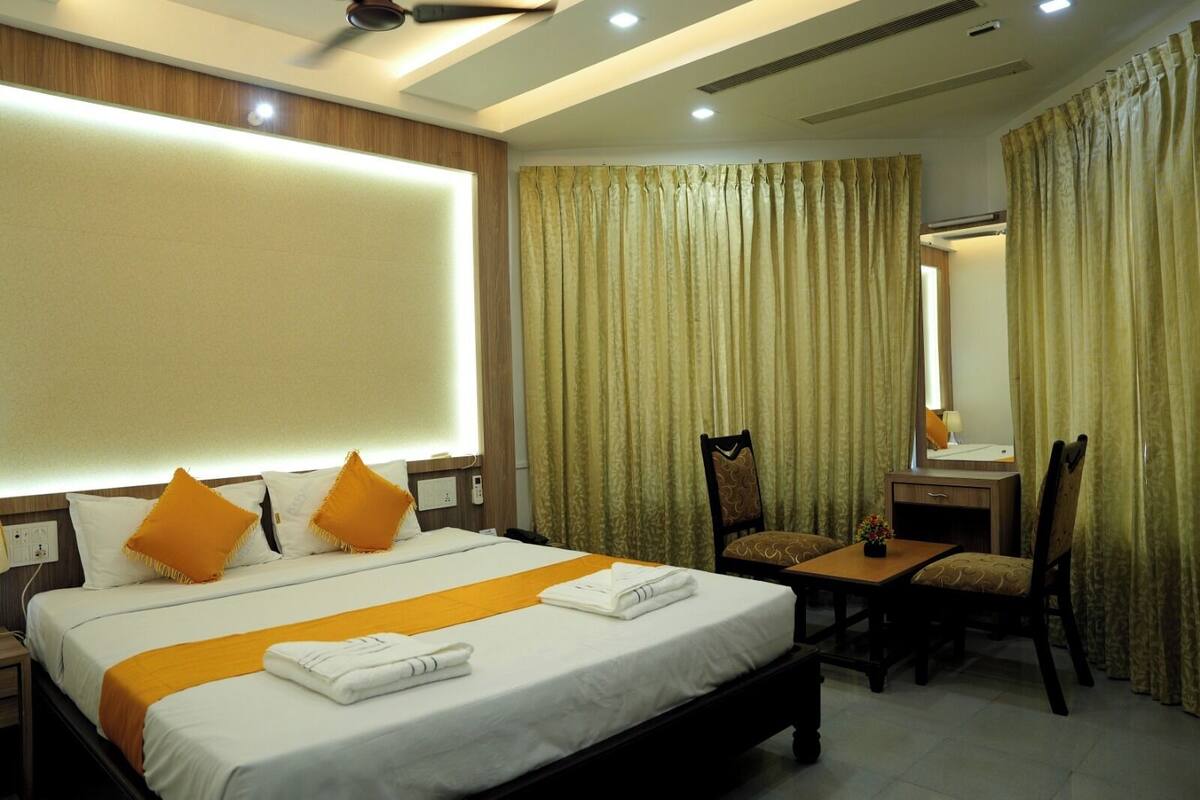 Quarto de hotel com uma cama grande, duas cadeiras, uma escrivaninha e um espelho.