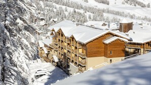 Uma cabana de madeira com várias varandas e um telhado coberto de neve, emoldurada por uma paisagem montanhosa nevada.