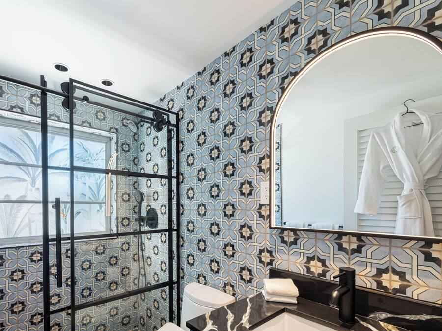 Casa de banho com azulejos estampados, cabine de chuveiro em vidro, espelho grande e toalha sobre o balcão.