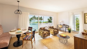 Uma sala de estar moderna com área de jantar, um conjunto de sofá, uma mesinha com abajur e vista para o oceano.
