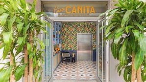 Entrada de hotel com placa indicando 'Casa CANITA', piso de azulejos, um banco e plantas em vasos.