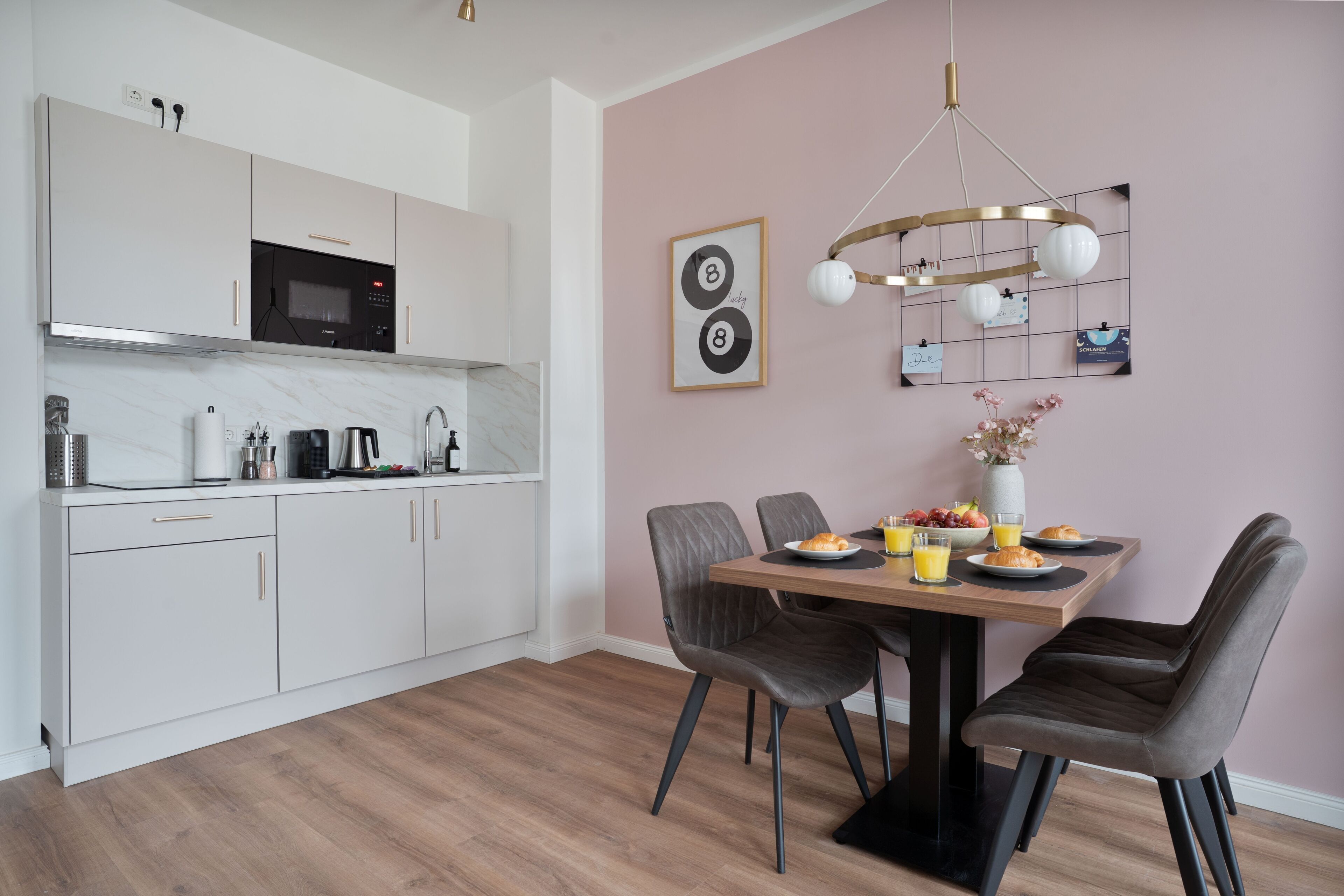Uma cozinha moderna com armários brancos, micro-ondas e um espaço de jantar com mesa posta para dois.