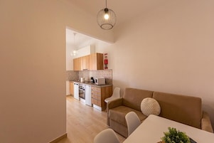 Uma sala de estar moderna com um sofá, uma mesa de jantar e uma cozinha ao fundo.
