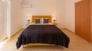 Quarto com cama, luminárias de cabeceira, porta de madeira e ar condicionado.