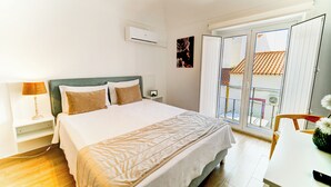 Quarto com cama, mesa de cabeceira, abajur e vista para a varanda.
