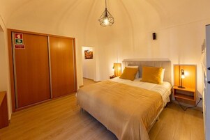 Quarto de hotel com uma cama grande, guarda-roupa de madeira, abajures e um candeeiro no teto.