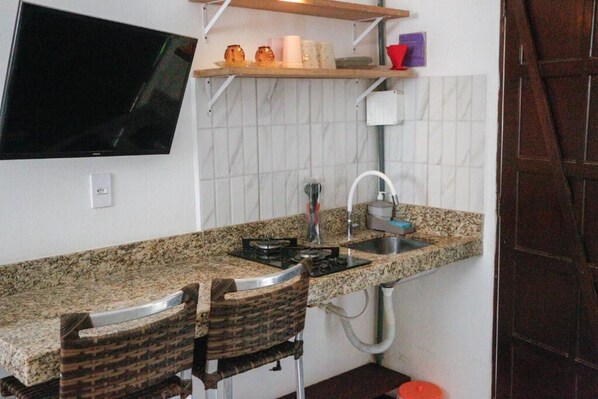Uma cozinha compacta com bancada de granito, fogão embutido, pia e TV fixada na parede.