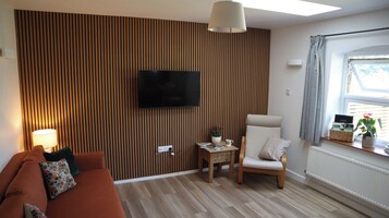 Uma sala de estar moderna com sofá, poltrona, televisão e uma janela com cortinas.