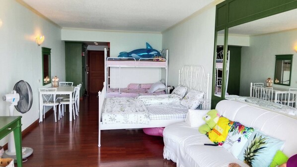 Um quarto com uma cama beliche, uma mesa de jantar com cadeiras, um sofá branco com almofadas coloridas e um espelho grande.