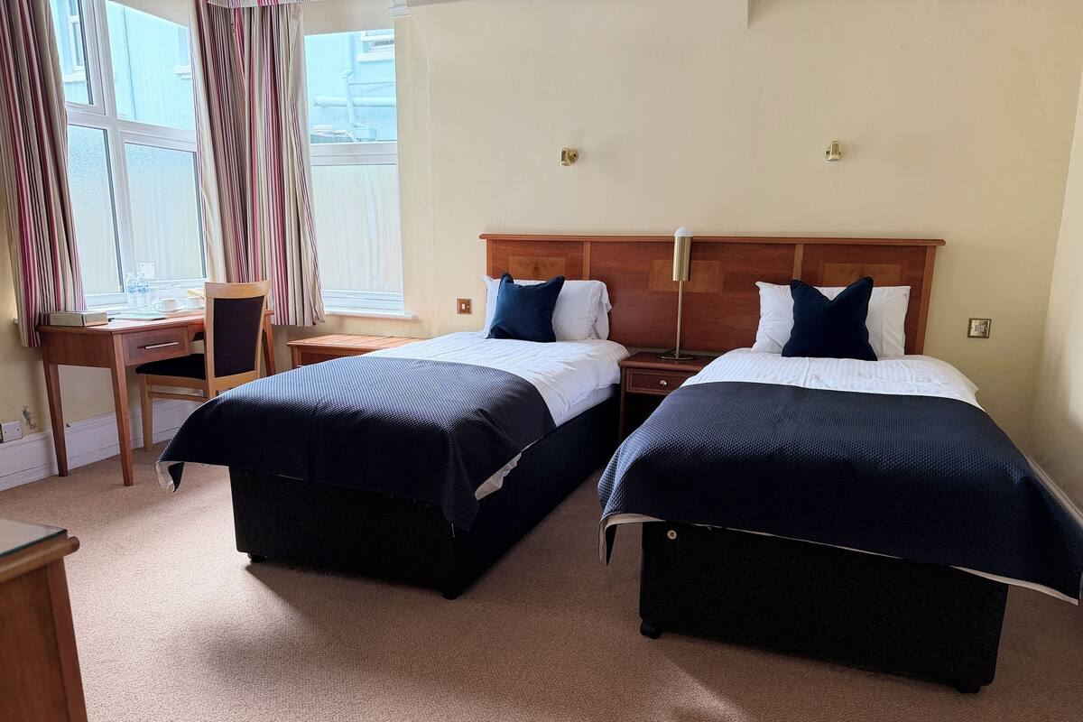 Quarto de hotel com duas camas, uma escrivaninha e uma cadeira.