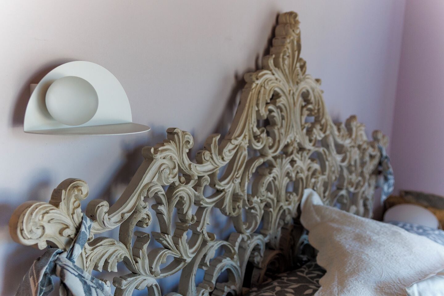 Uma cama com cabeceira ornamentada, um travesseiro branco e um adorno de parede decorativo.