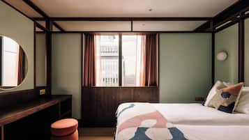 Quarto de hotel com uma cama grande, um banco de madeira, um espelho redondo e uma janela com cortinas.