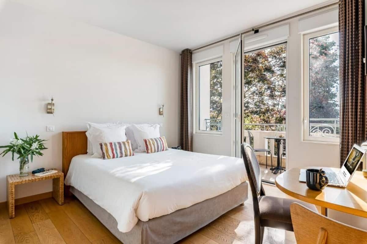 Um quarto com cama, mesa de cabeceira e um laptop em uma escrivaninha.