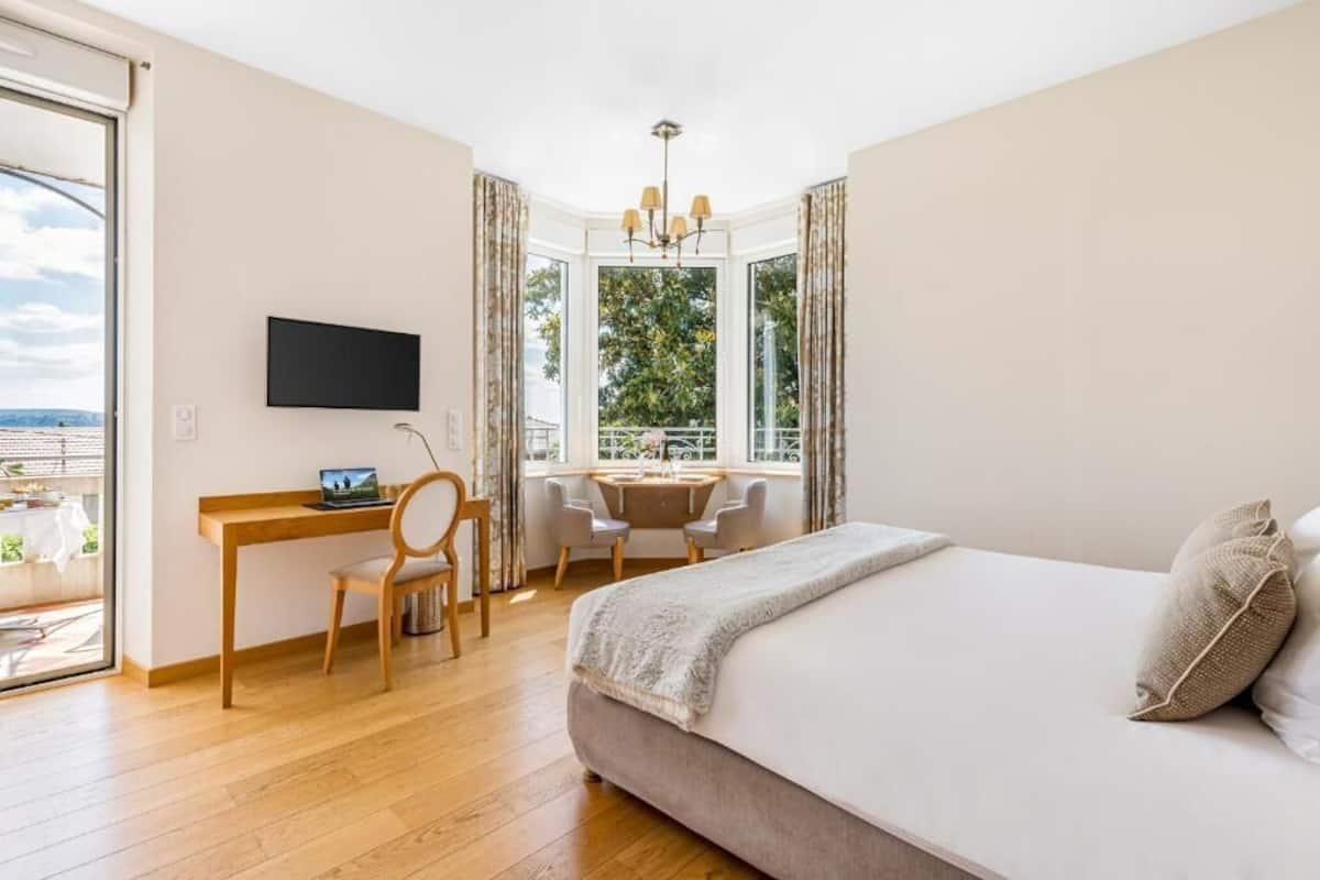 Quarto com cama, escrivaninha, cadeira, televisão e varanda com vista.