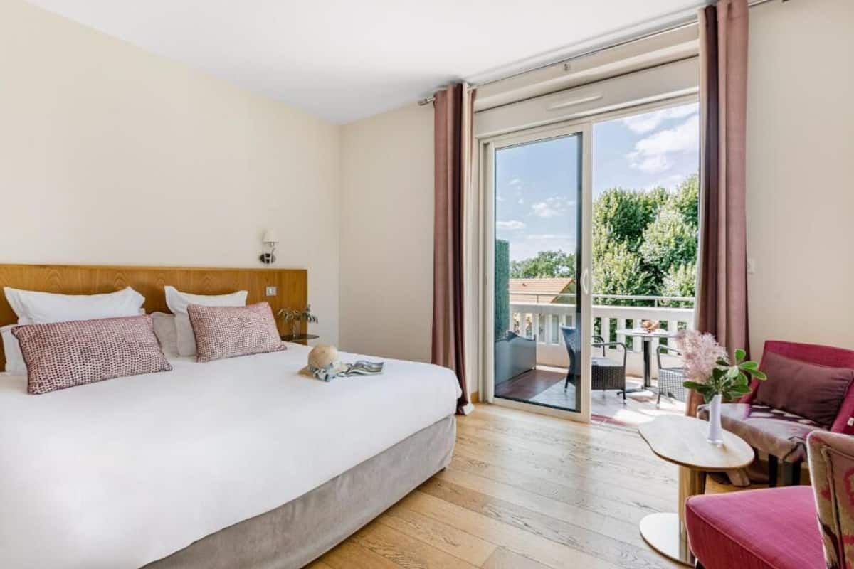 Quarto de hotel com uma cama grande, uma mesinha, uma cadeira e varanda com área de estar ao ar livre.