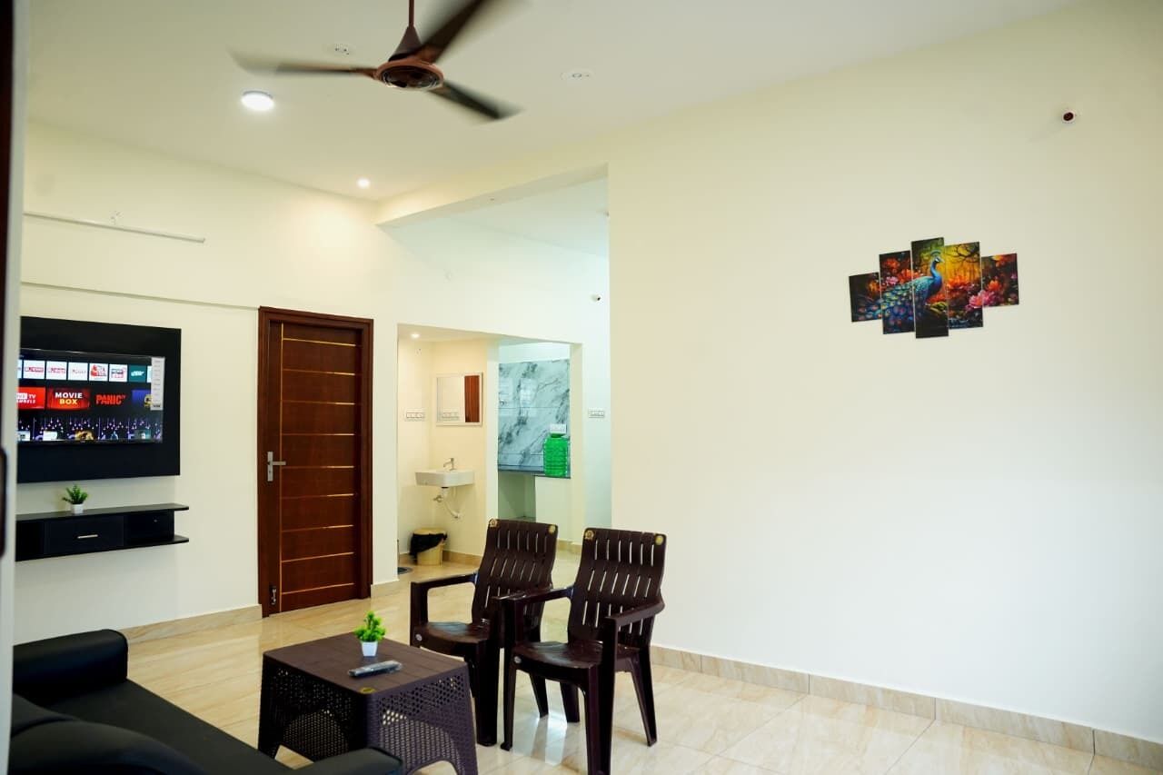 Sala de estar com televisão de tela plana, ventilador de teto, sofá, mesa de centro e uma obra de arte pendurada na parede.