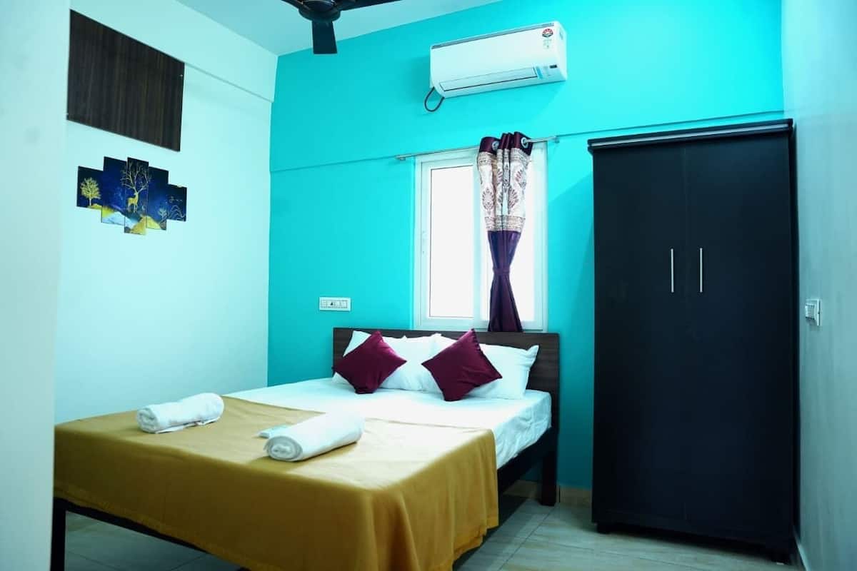 Quarto com cama, guarda-roupa, ar-condicionado e janela com cortinas.