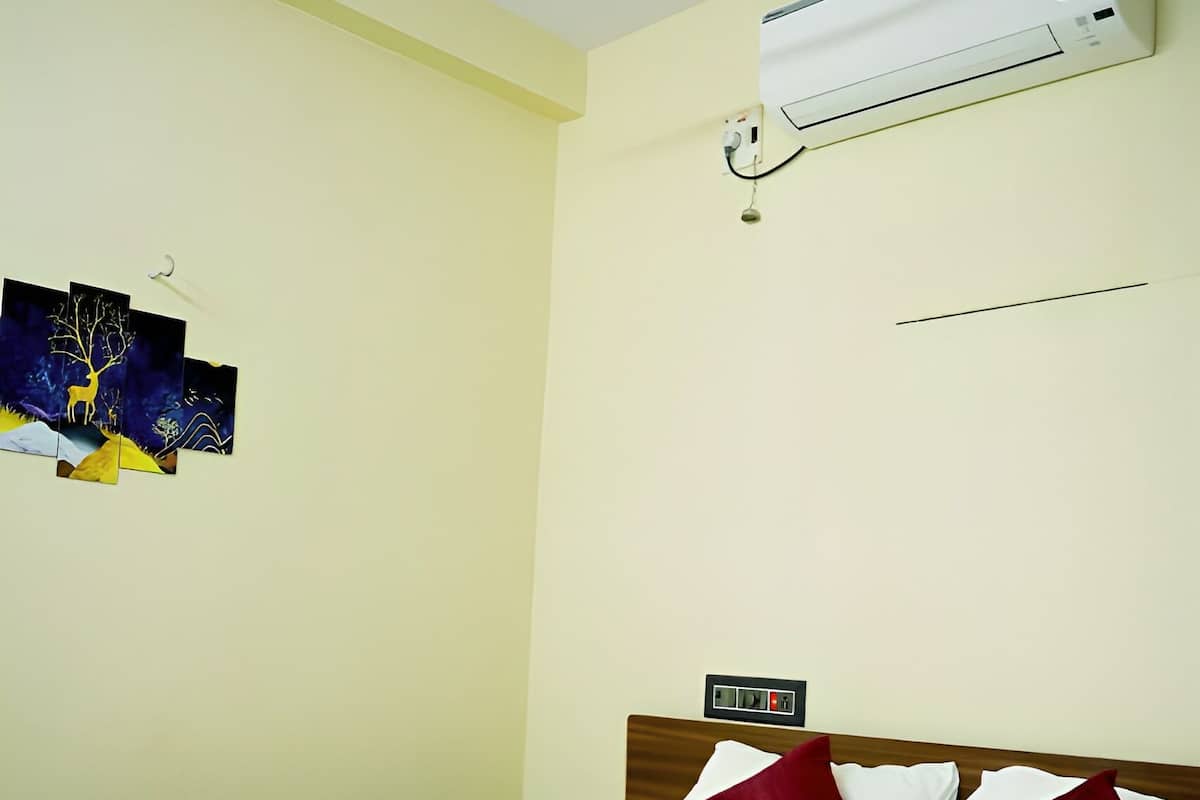 Quarto de hotel com cama, roupa de cama branca, almofadas vermelhas, unidade de ar condicionado e painel de controle fixado na parede.