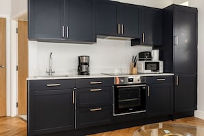 Cozinha moderna com armários pretos, eletrodomésticos de aço inoxidável e mesa com tampo de vidro.