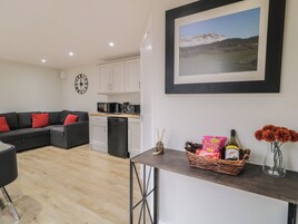 Uma sala de estar moderna com um sofá cinzento, uma mesa de jantar e uma cozinha com armários brancos e uma máquina de lavar louça.