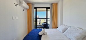 Quarto de hotel com cama, janela com cortinas, aparelho de ar condicionado e vista para edifícios.